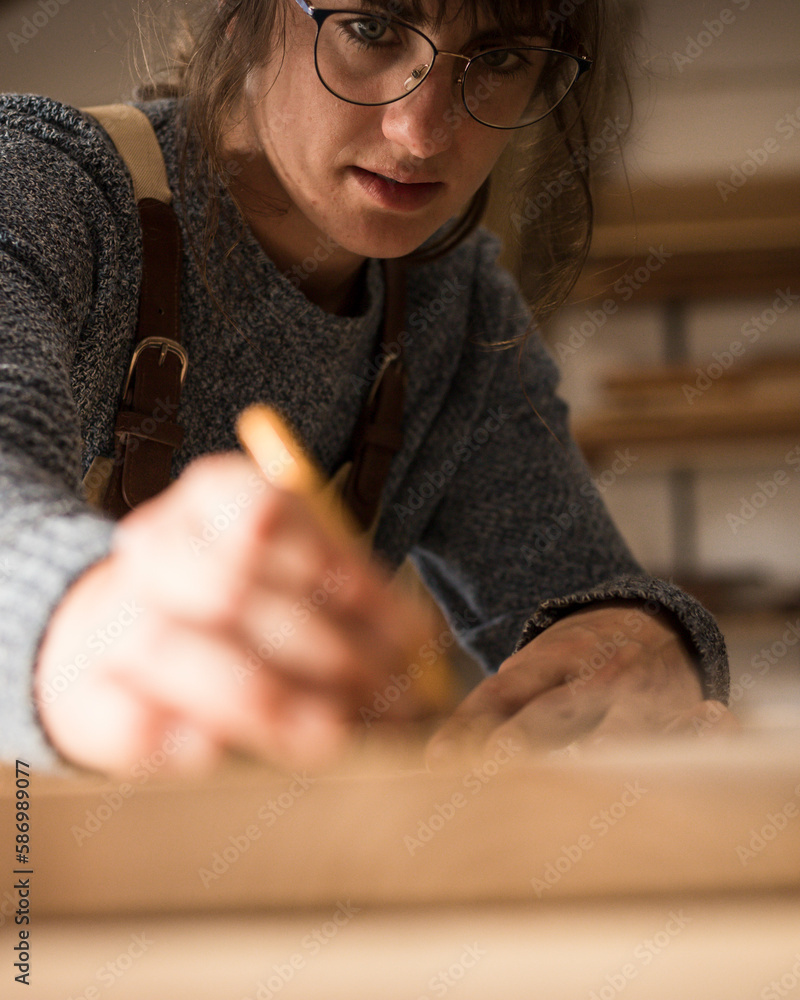 A young female carpenter working as wood designer in a small carpentry ...