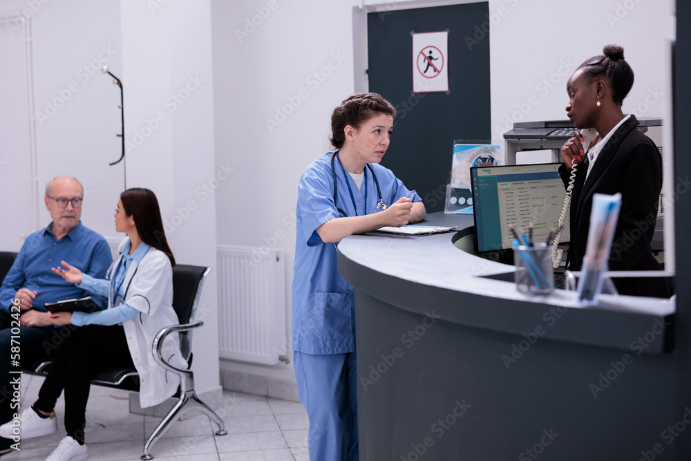 Nurse standing at counter desk discussing with receptionist during ...