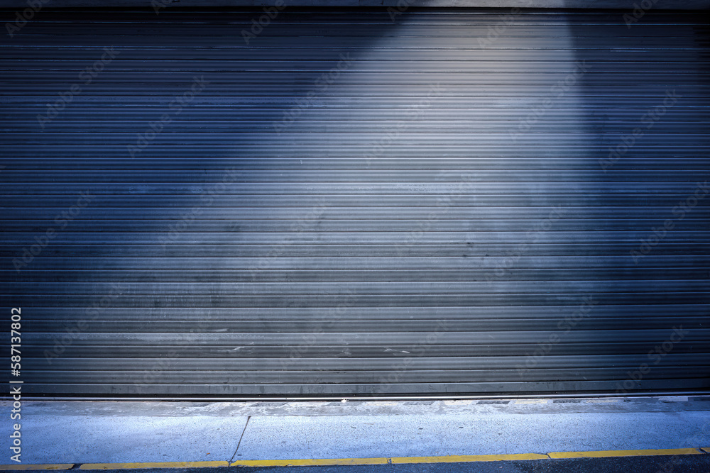 Frontal view of a closed metal roller shutter at night with a sidewalk ...