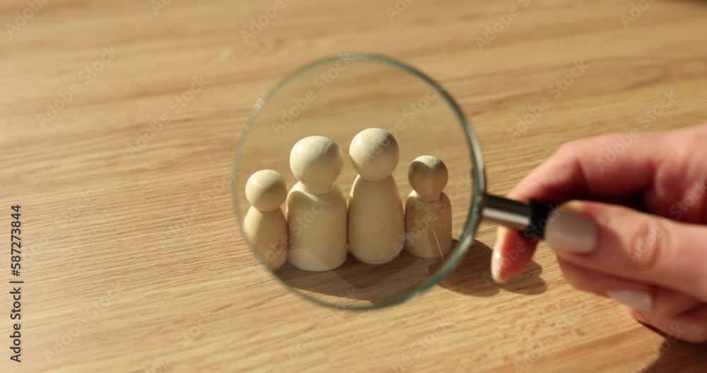 Magnifying glass looks at wooden figurines of family. Traditional ...