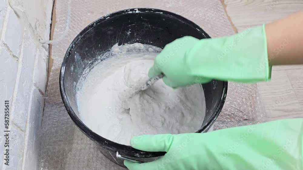 The hand of the master stir the plaster in a bucket with a spatula ...