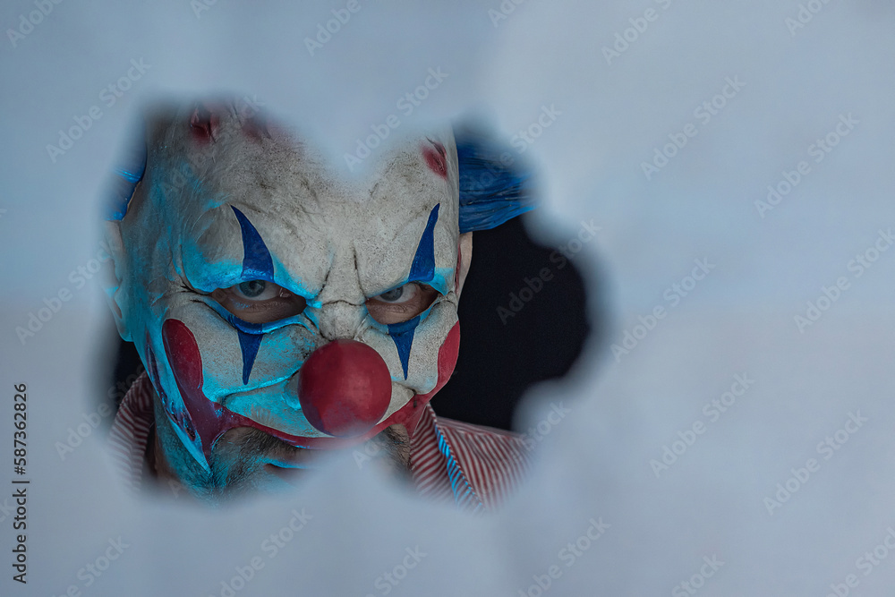 Scary clown face looking through the hole in close-up. The face of a ...