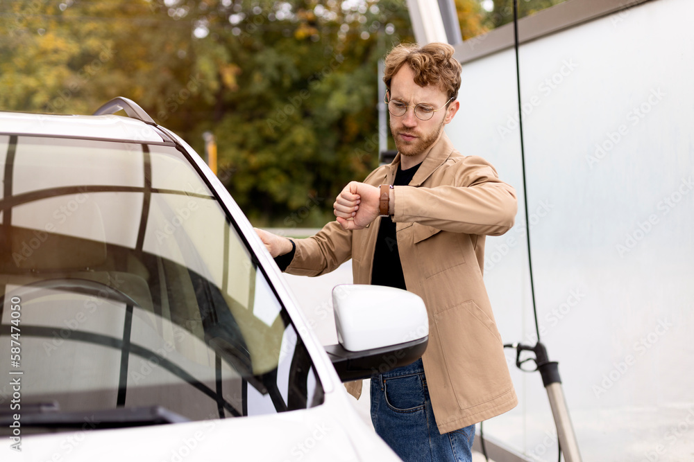 Handsome busy man driver looking at watch, checking time standing near ...