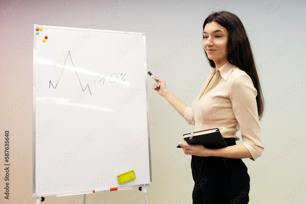 Beautiful woman drawing graph on flip chart, holding a notebook ...