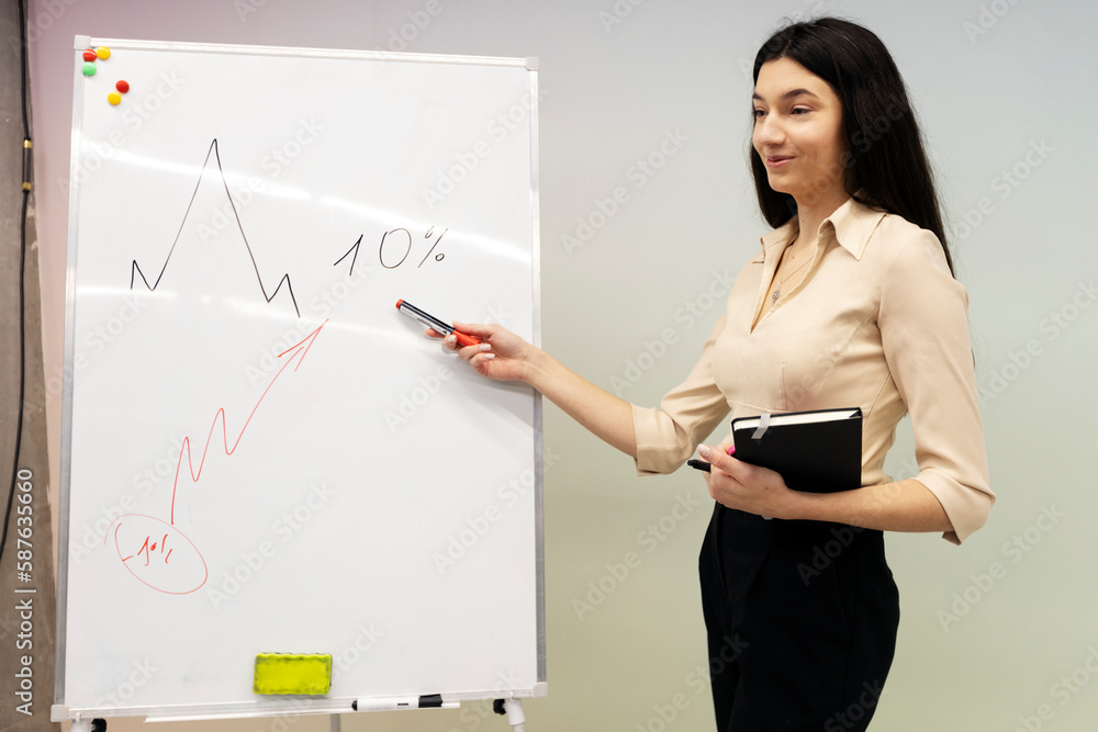 Woman drawing graph on flip chart, holding notebook, pointing. Work ...