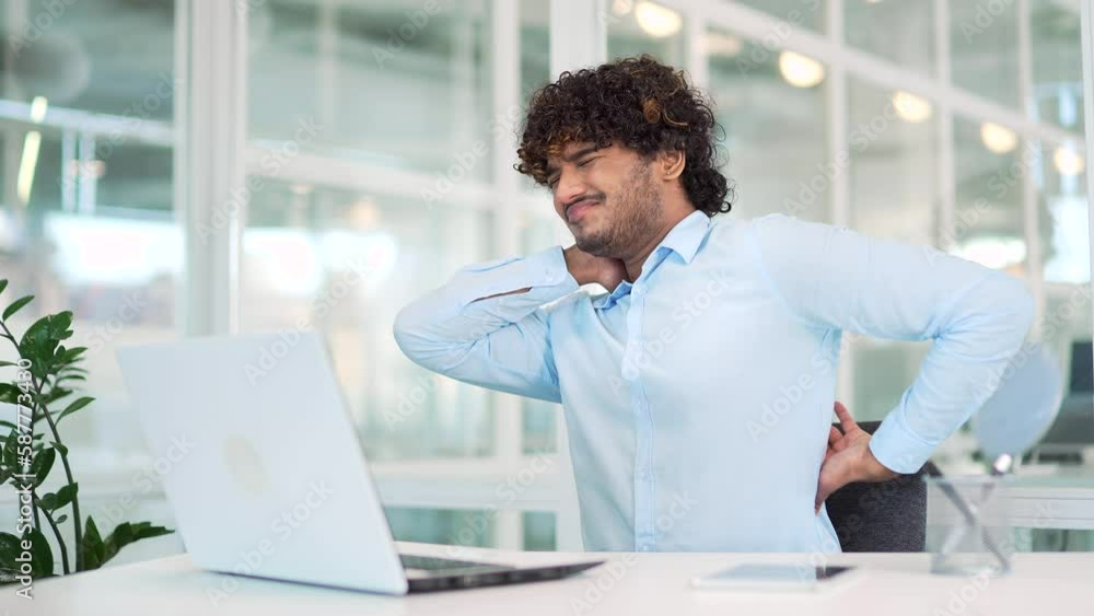 Tired young man suffering from neck and back pain while working on ...
