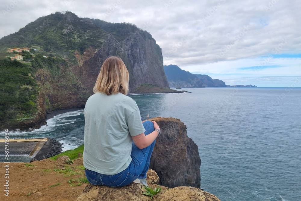 Foto de The girl sits on a mountainside and looks at the sea or ocean ...