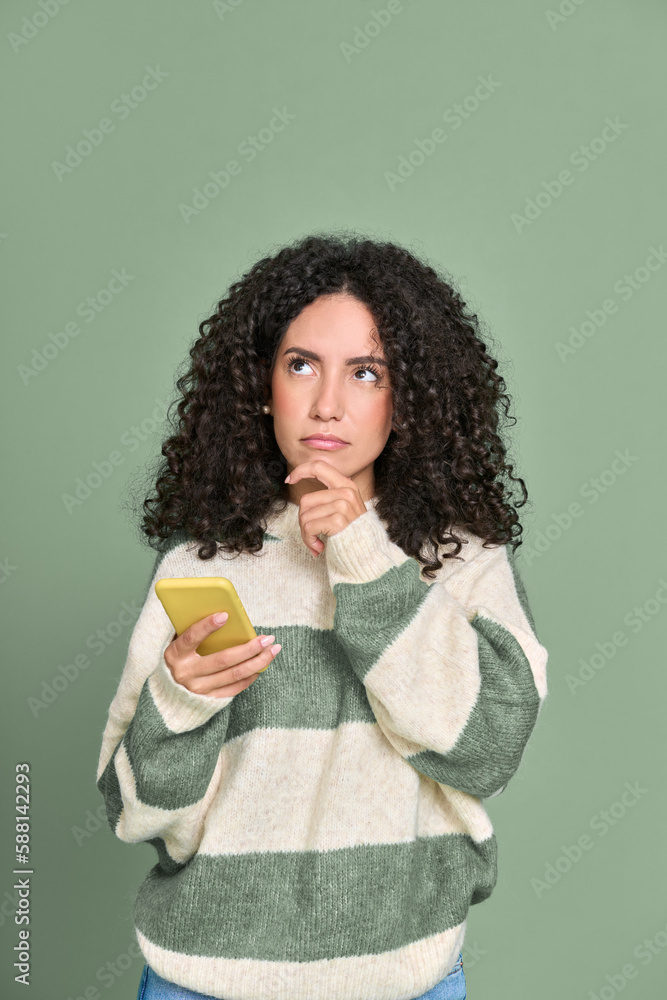 Young thoughtful unsure latin woman holding hand on chin using mobile ...