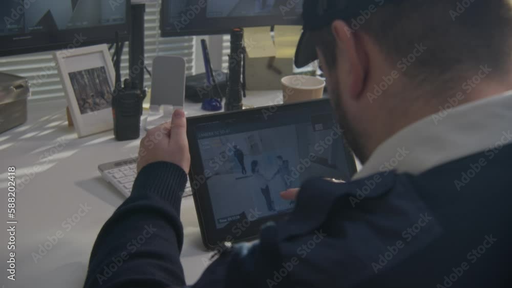 Security guard monitors CCTV cameras in office on digital tablet ...