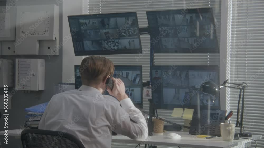 Security guard controls office CCTV cameras on computers, uses walkie ...