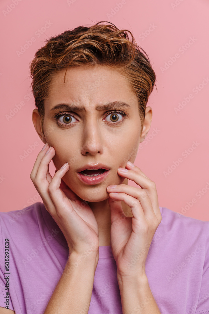 Young short-haired beautiful scared woman touching her cheeks lloking ...