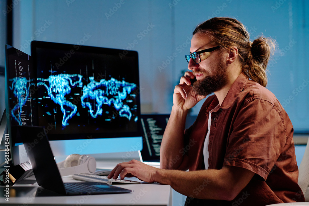 Side view of young busy male IT engineer giving consultation on mobile ...