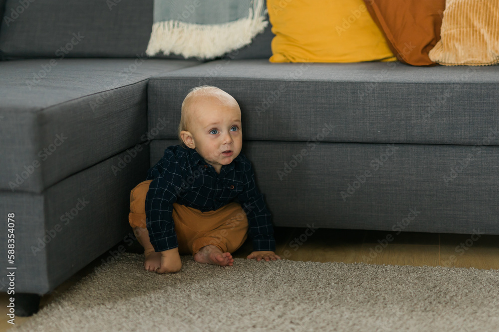 Frustrated scared toddler boy hiding behind a sofa copy space - concept ...