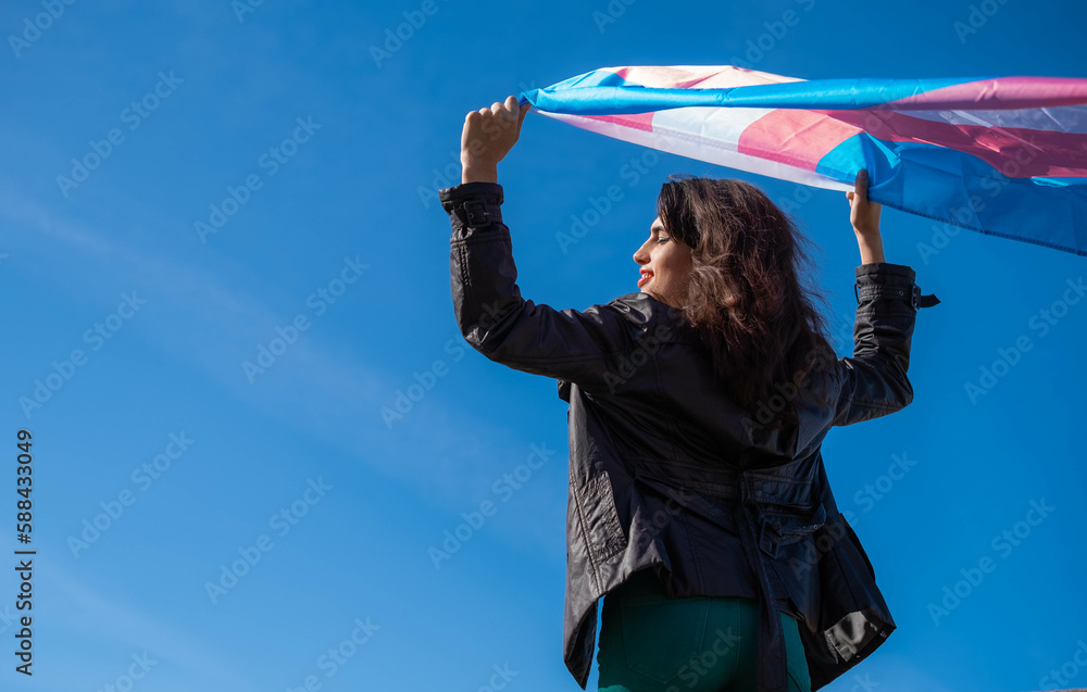 Transgender woman raising the trans flag in flight with a clear sky in ...