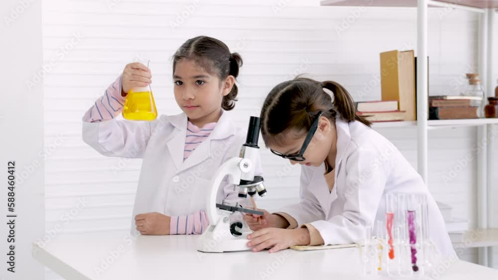Two elementary school girls wearing lab coats doing an experiment ...