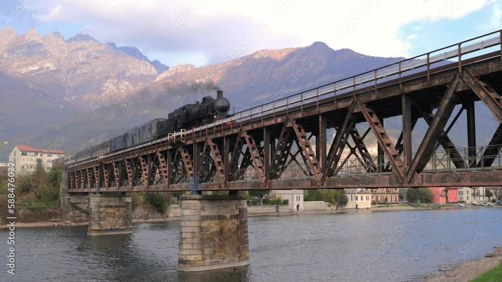 Ancient steam train crossing an ancient iron bridge over a river with ...