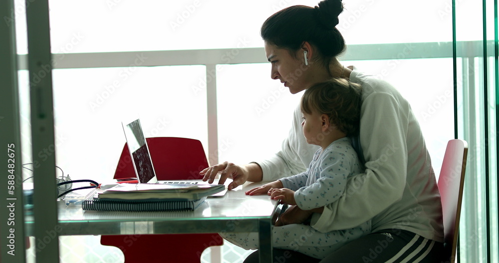 Mother multi-tasking, holding baby infant and using computer laptop at ...