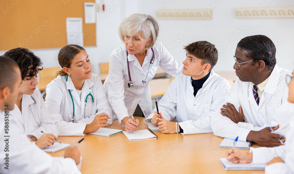 Elderly female doctor conducts training for interns of different ages ...