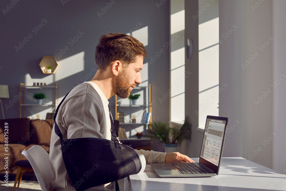 Man with broken arm working on laptop computer in office. Side view ...