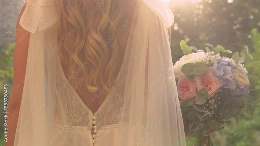 LENS FLARE, CLOSE UP: Back view of bride with bouquet walking towards ...