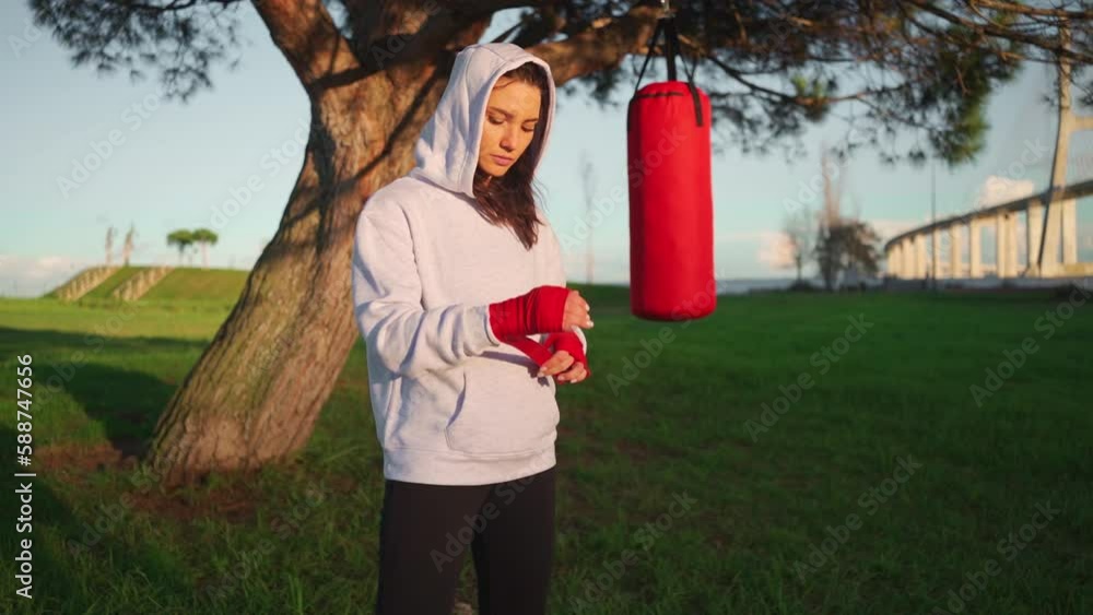 Female boxer standing in park near punching bag, looking in camera ...