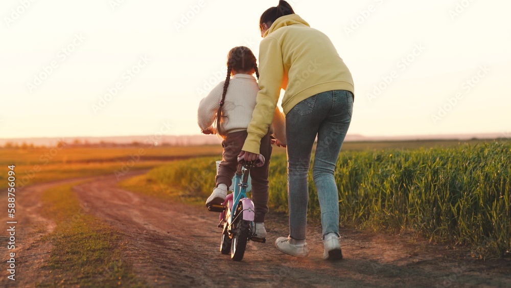 mother teaches child ride two-wheeled bicycle sunset. happy family ...