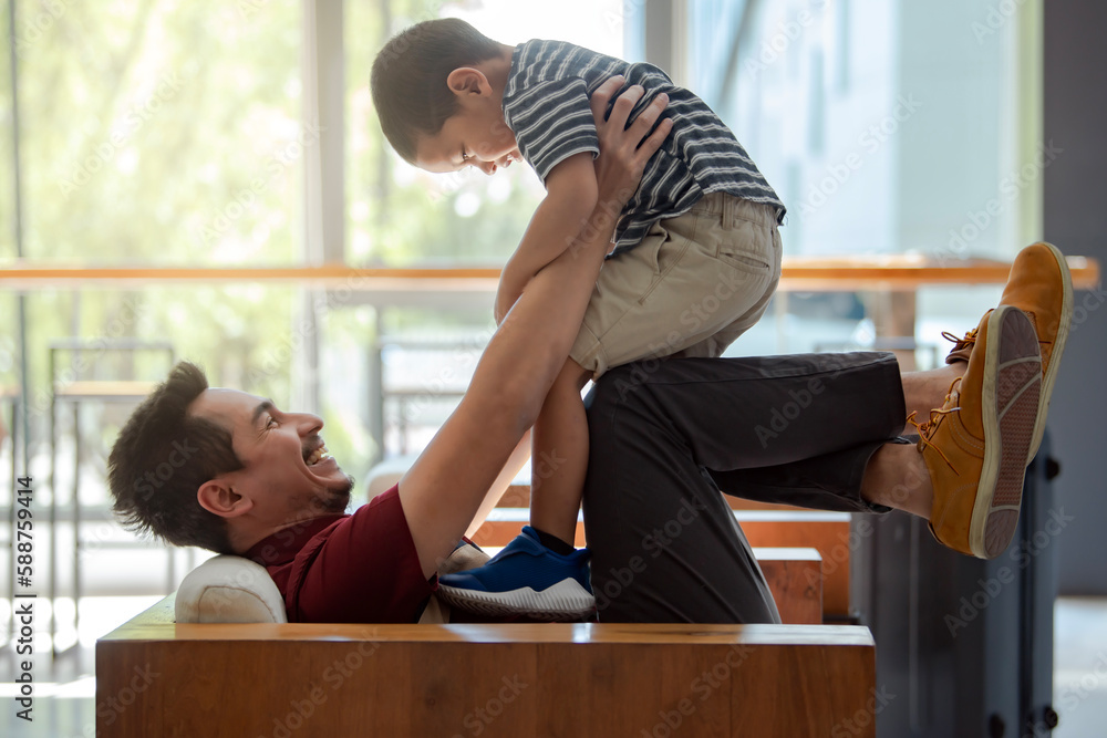Cheerful asian father sitting on sofa with suitcase and Little son ...