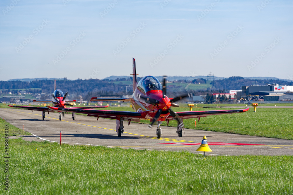 Two red and white Pilatus PC-21 propeller airplanes taxiing to runway ...