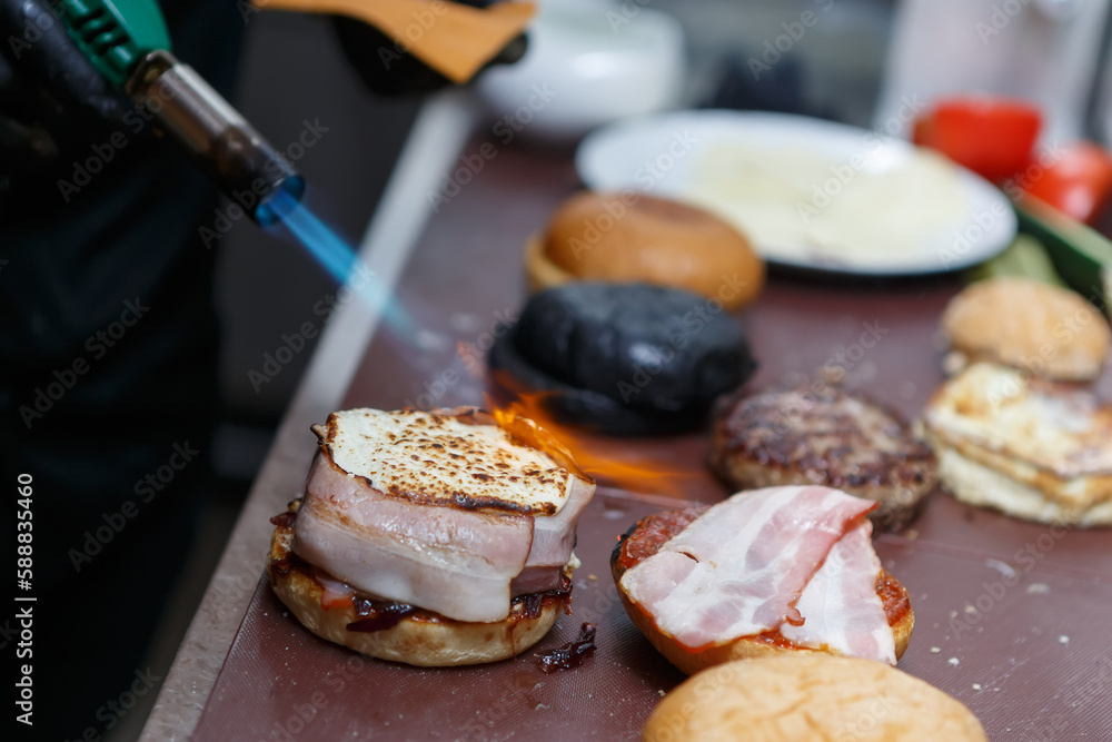 Cook using burner flame to prepared burger in a restaurant kitchen ...