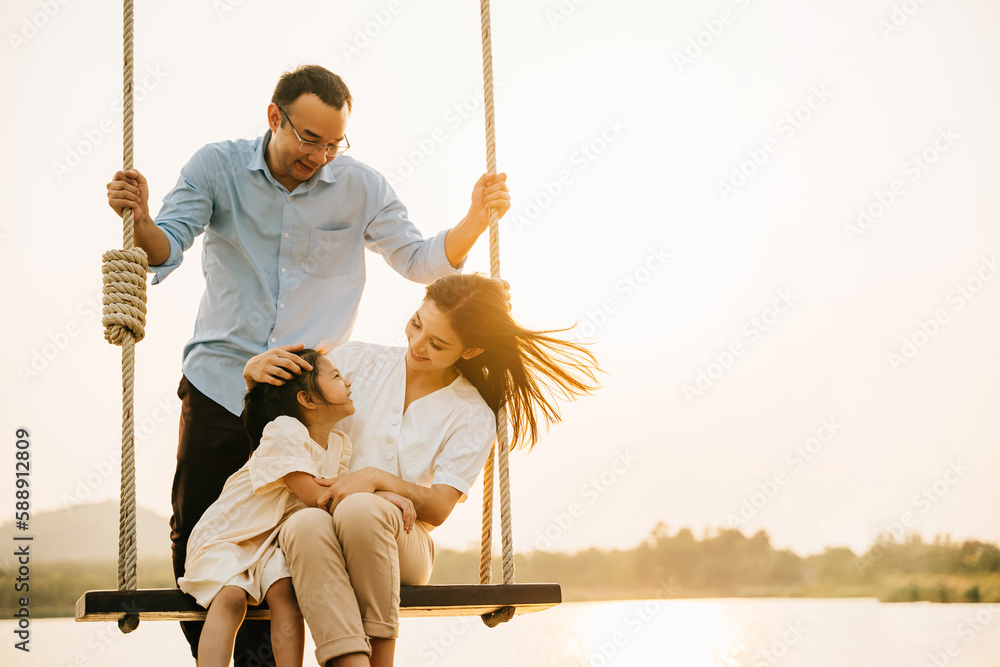 A happy family playing together on a swing set in a beautiful park ...