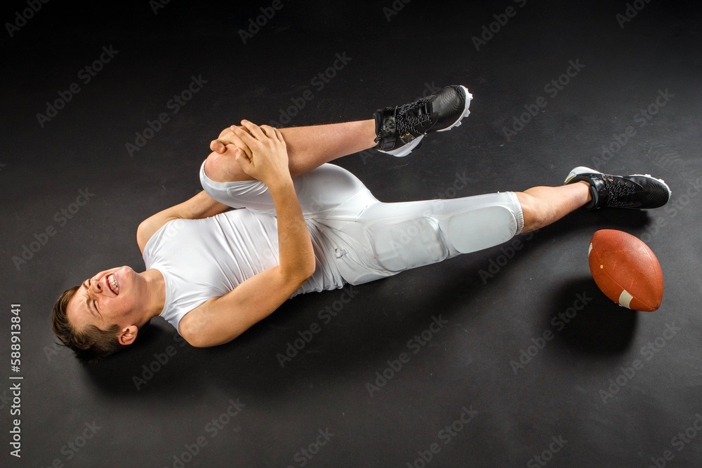 Young preteen football boy in football uniform laying injured on studio ...