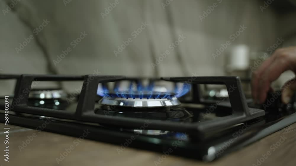 On gas kitchen stove, man hand turns knob and opens gas supply, blue ...