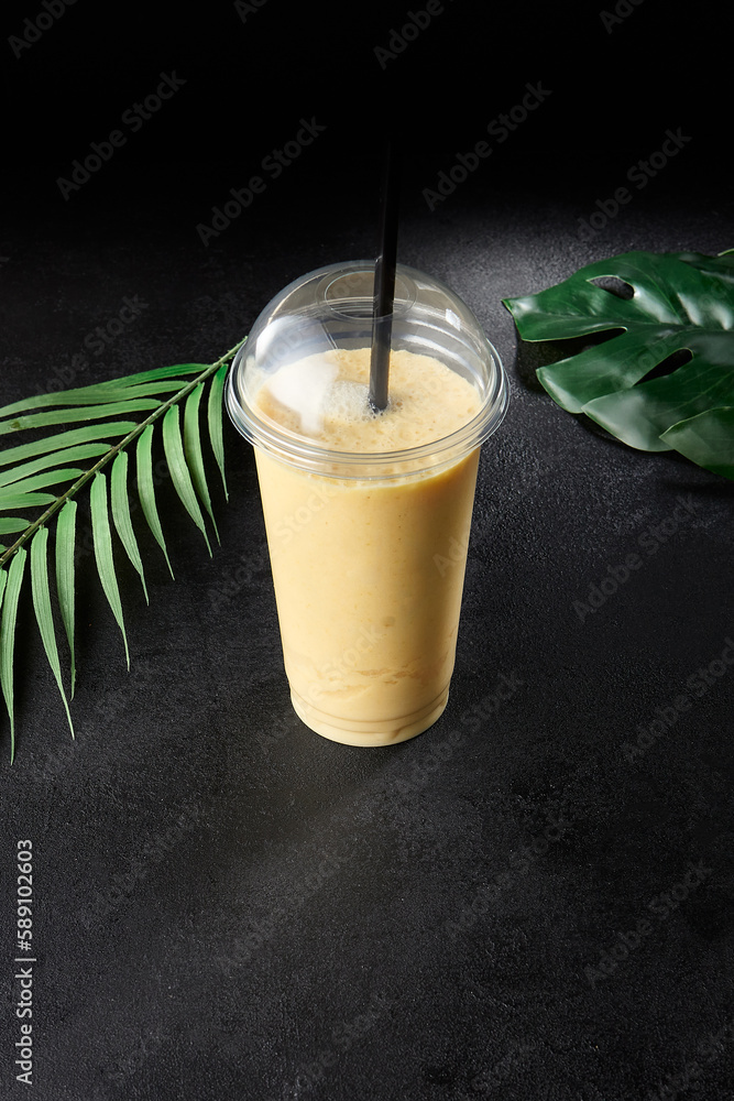 Mango shake in take out glass on dark background with leaves. Mock up ...