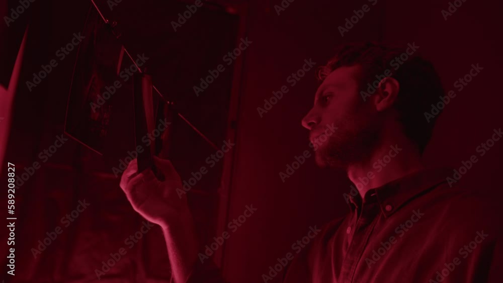 man is hanging and looking at photos in a dark room with red lights. He ...