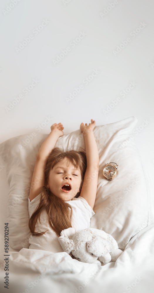 Cute funny cheerful little girl with brown hair wakes up on the morning ...