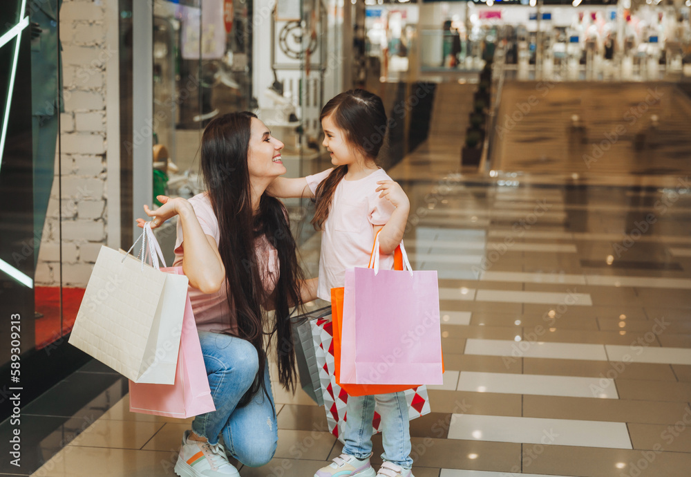 young mother and daughter holding shopping bags, shopping in the mall ...