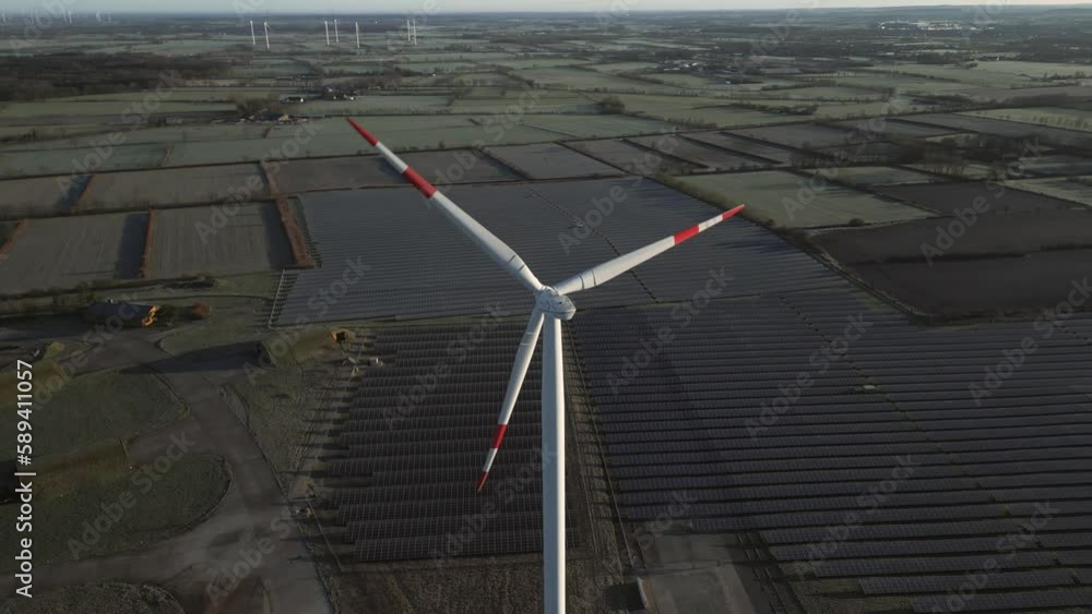 A wind turbine towering above a vast solar field in this video. The ...