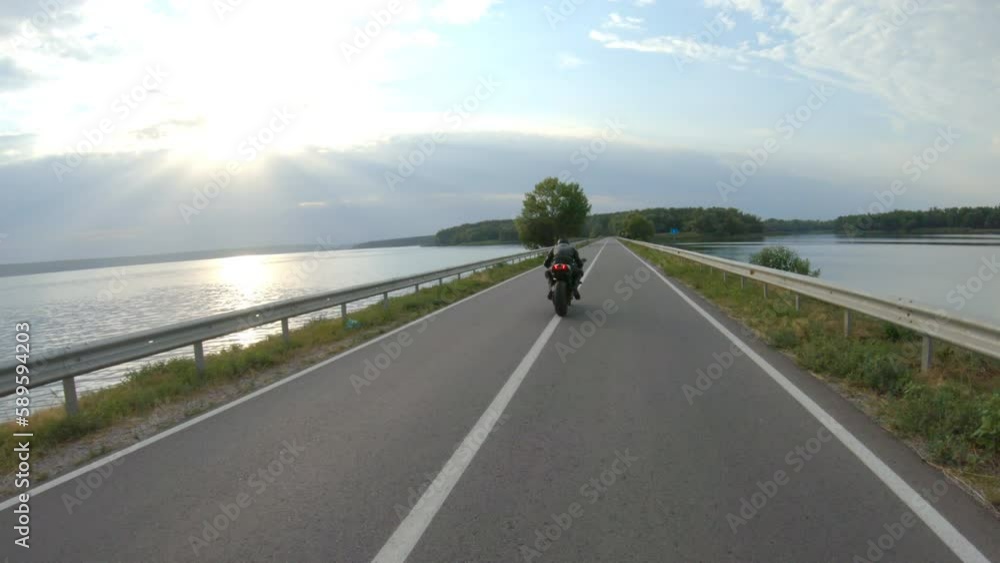 Biker riding on modern sport motorbike through road near lake ...