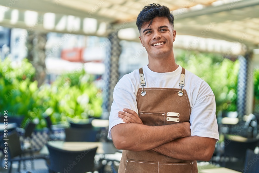 Young hispanic man waiter smiling confident standing with arms crossed ...