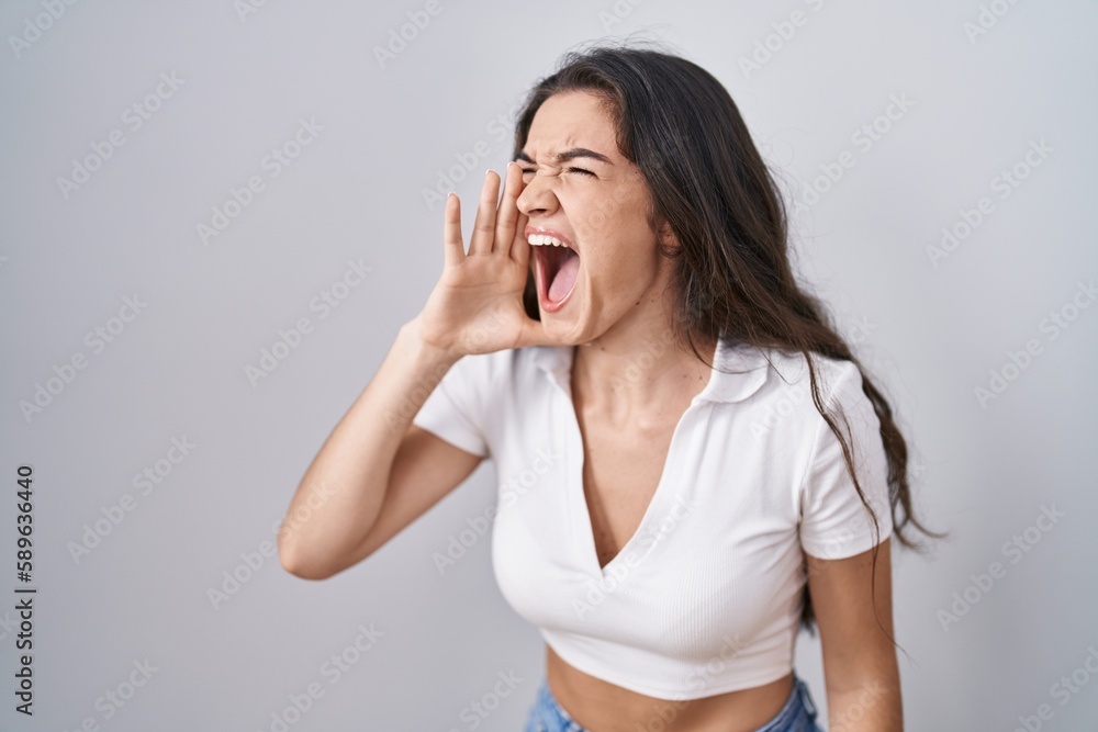 Young teenager girl standing over white background shouting and ...