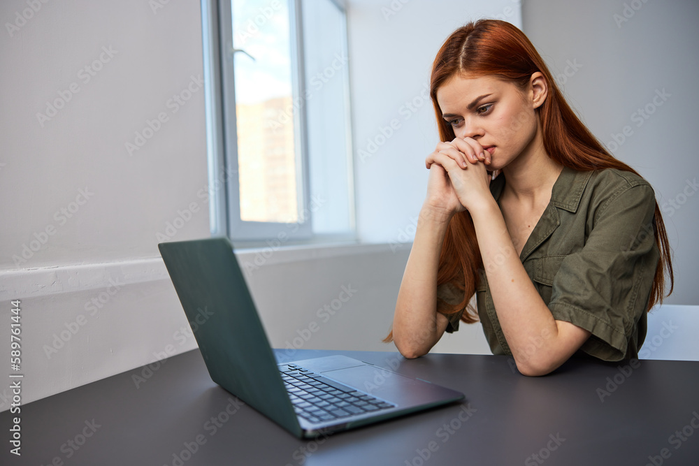 a serious, work-weary woman, with a sad face, sits at a laptop with her ...