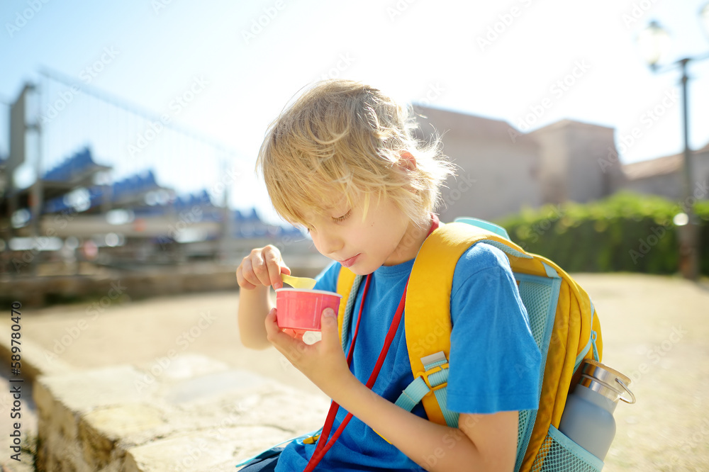 Happy little boy eating tasty ice cream in paper cup outdoors. School ...