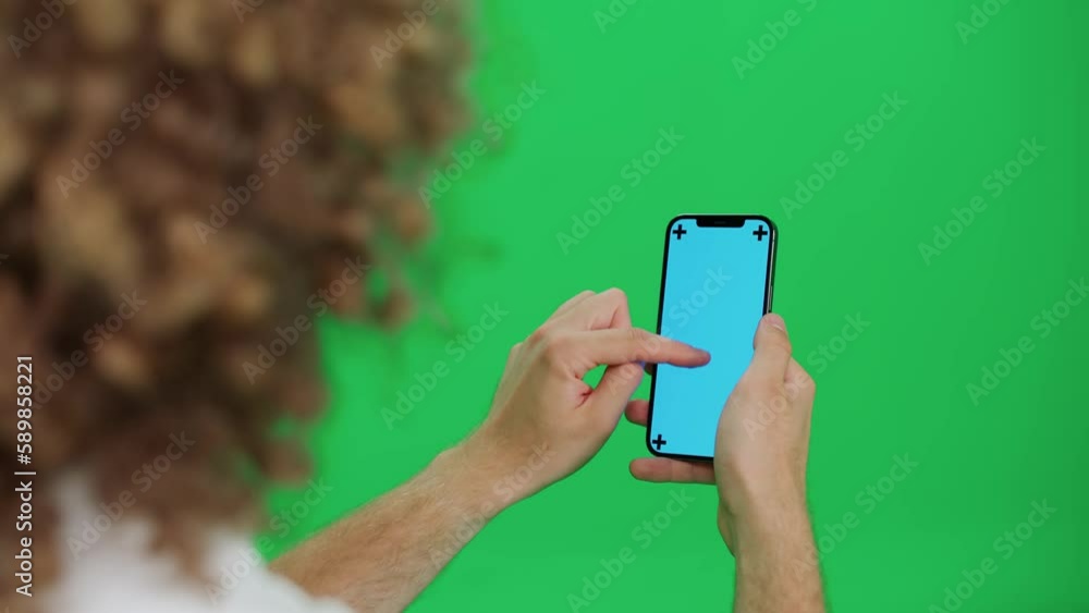 Back view, young man uses smartphone, scrolls through the images and ...