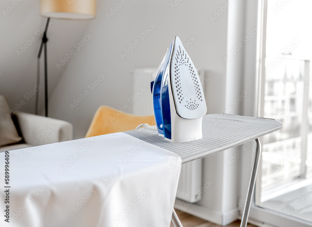 Electrical iron for wrinkled clothes on ironing board indoor. Modern ...