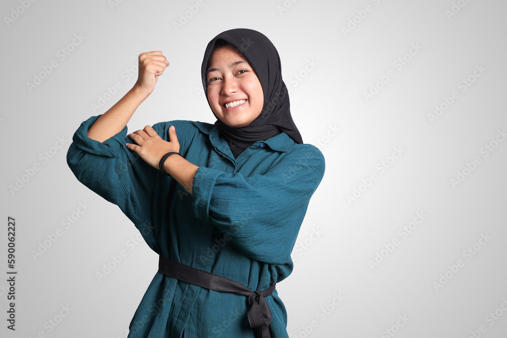 Portrait of excited Asian muslim woman with hijab showing strong biceps ...
