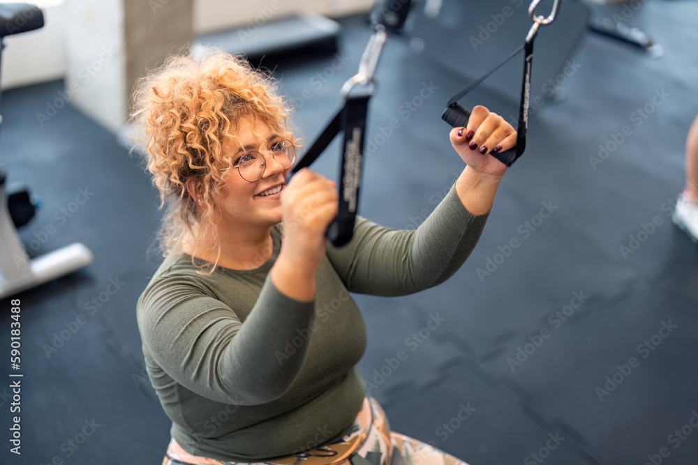Confident young woman exercising in gym, doing cable pulldowns weight ...
