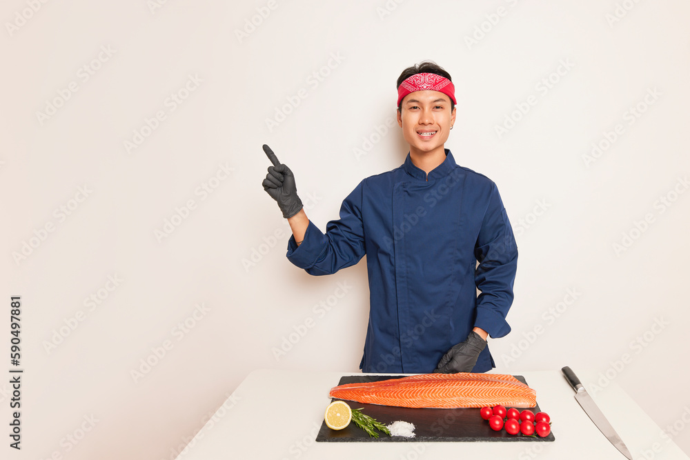 Young smailing chef in blue uniform posing at the cookong table with ...