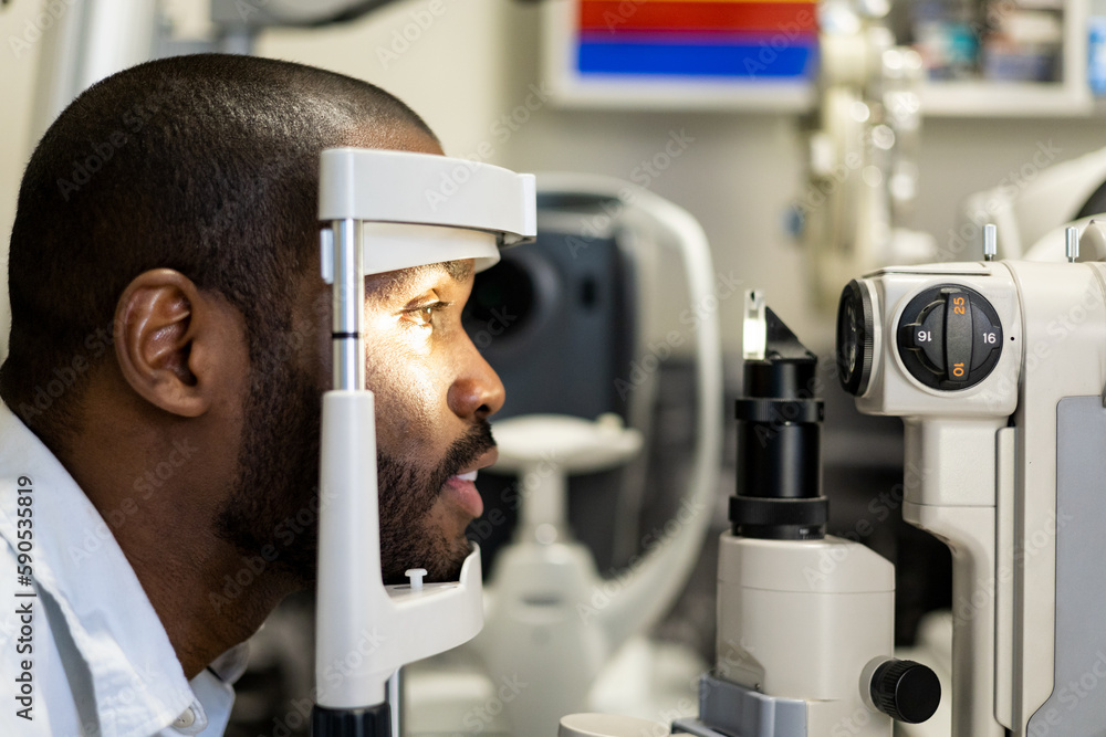 Profile view. Examination of a dark-skinned man with a slit lamp ...