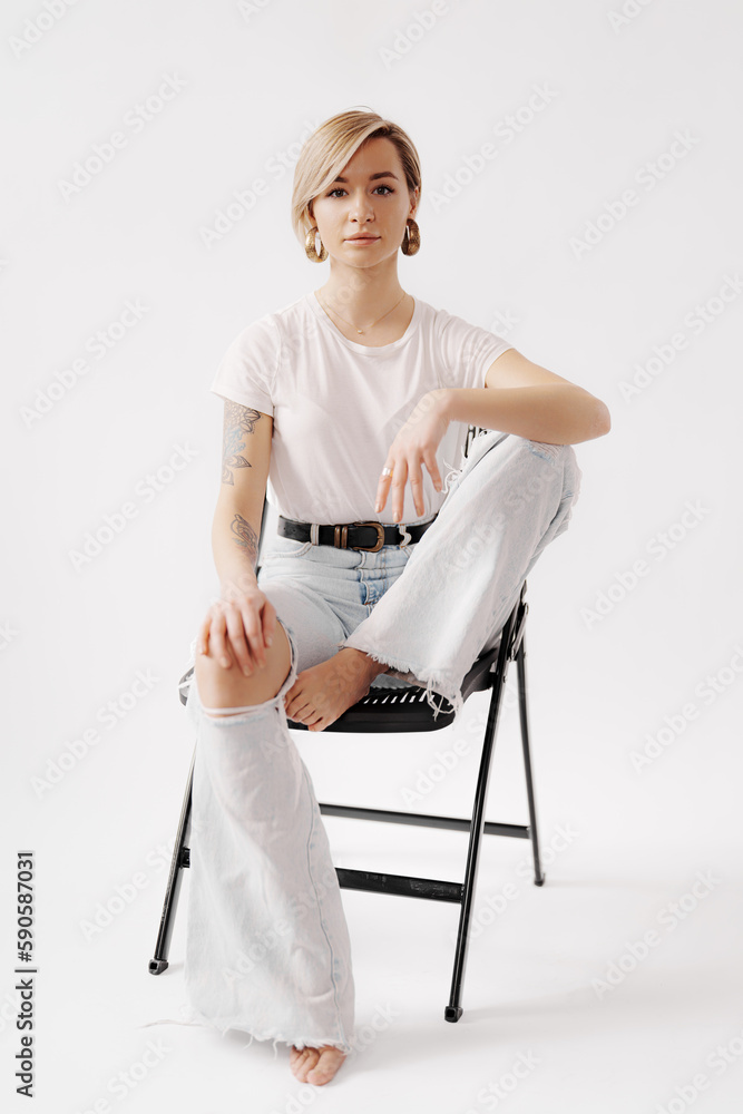 Full body of barefoot young female sitting with raised leg on chair and ...