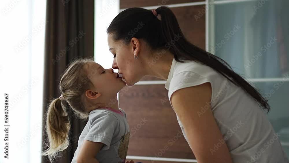 Young mother kissing her little daughter in the bedroom. Mommy and little girl spending time at ...